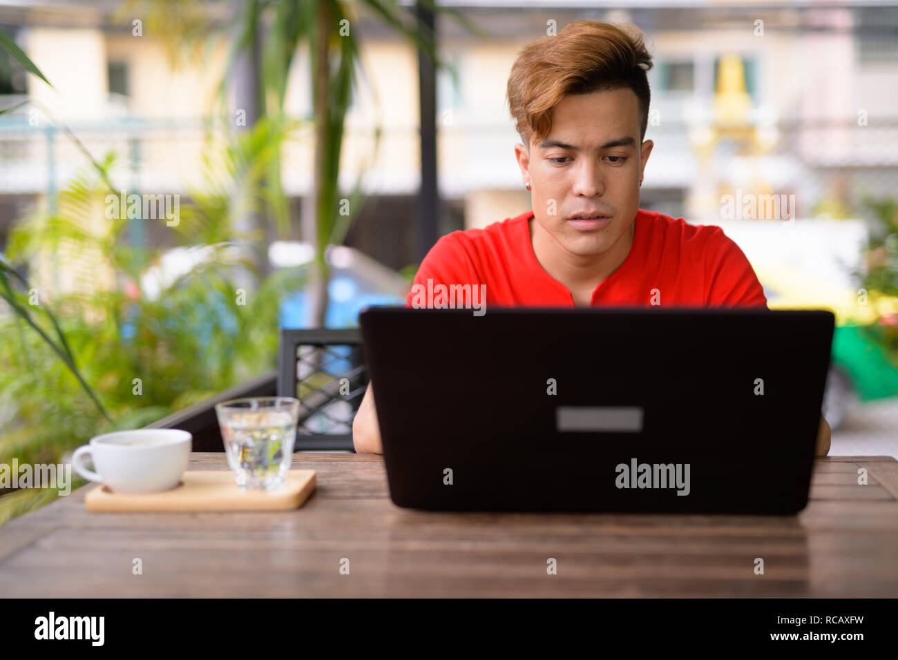 Young Asian man using laptop at the coffee shop outdoors Stock Photo ...