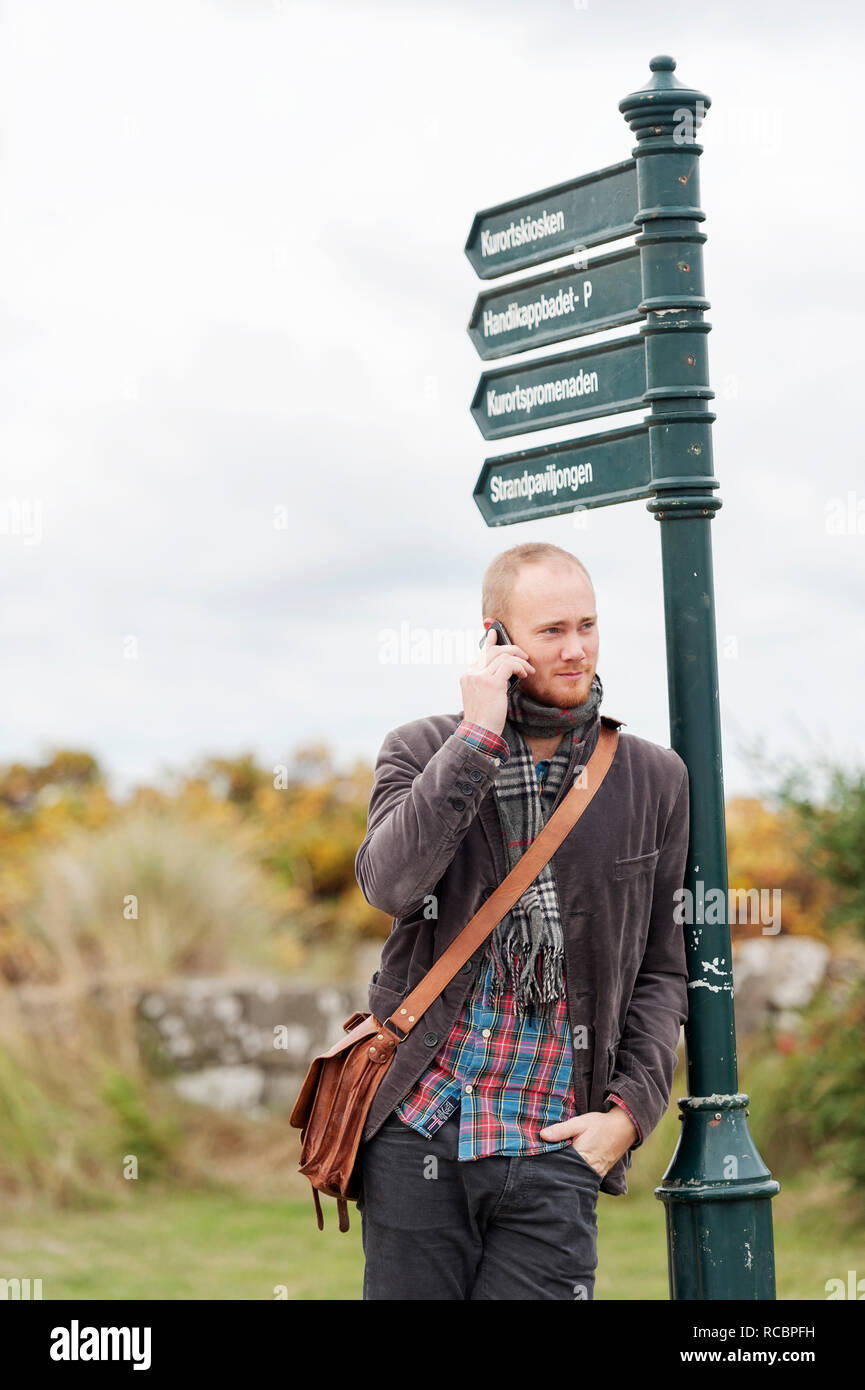 Young man talking by mobile phone next to directional sign Stock Photo ...