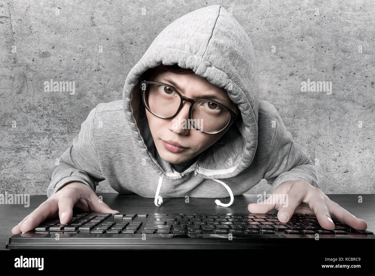a hacker (programmer) in a hood and glasses against a concrete wall ...