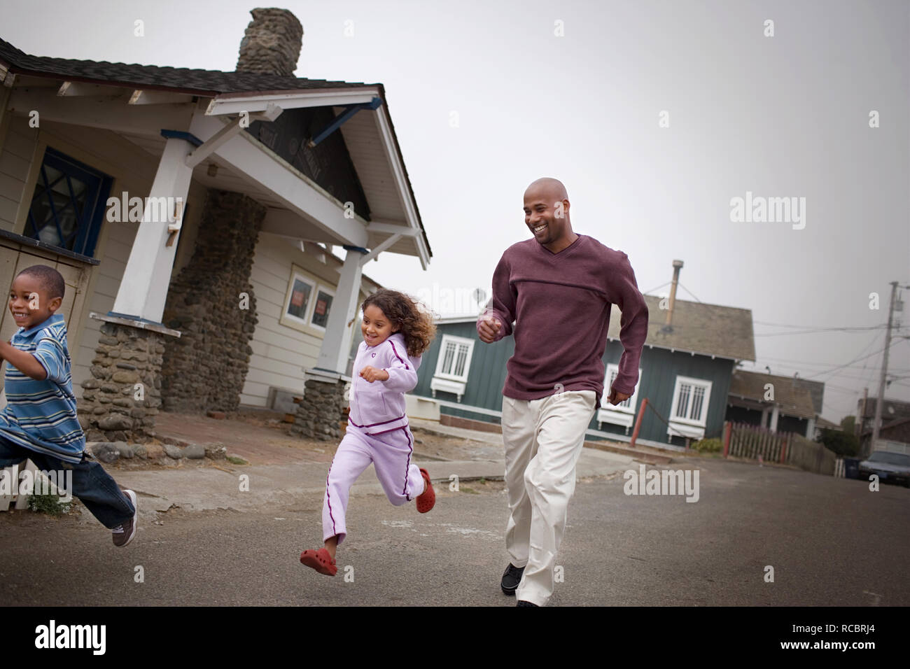 Smiling mid-adult father running down a suburban street with his two ...