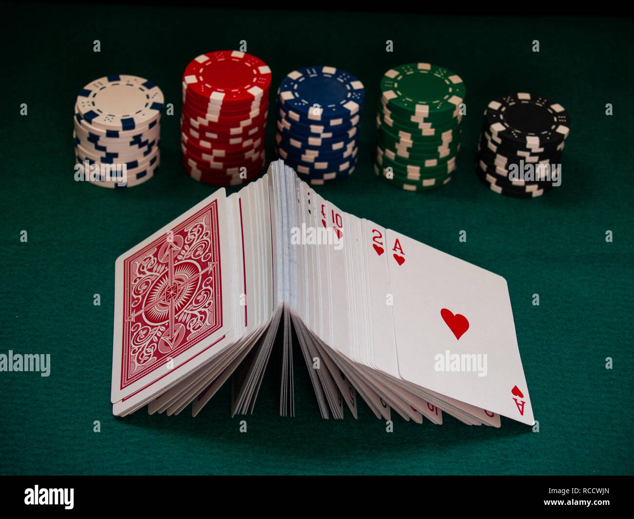 A deck of poker cards and poker chips of various colors on a green mat ...
