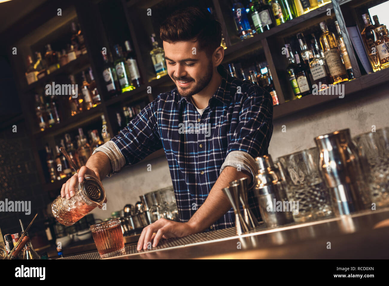 Young barman standing at bar counter pouring cold mix into glass ...