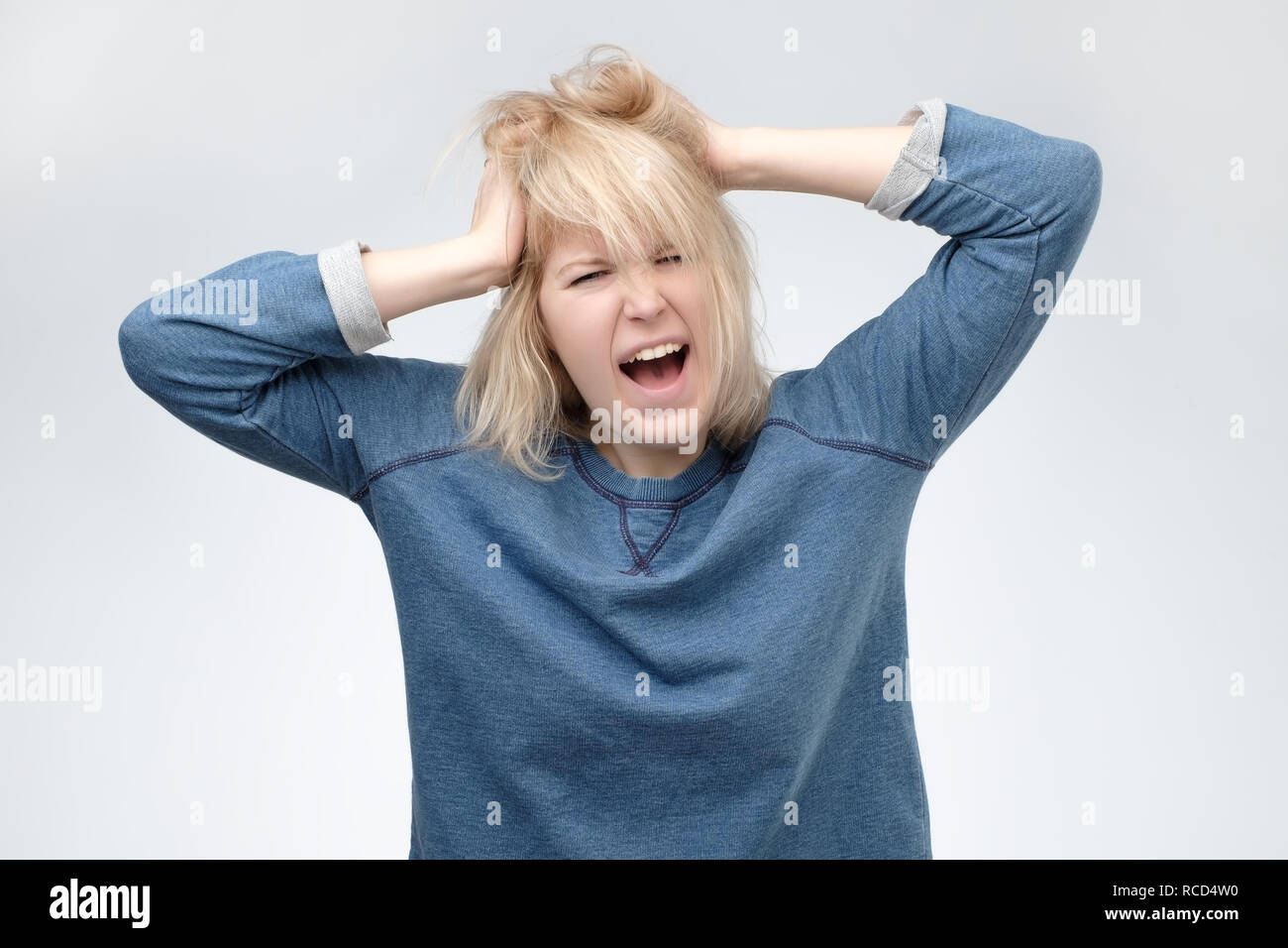 Shocked panic girl dressed in blue sweater holding hands on head and ...