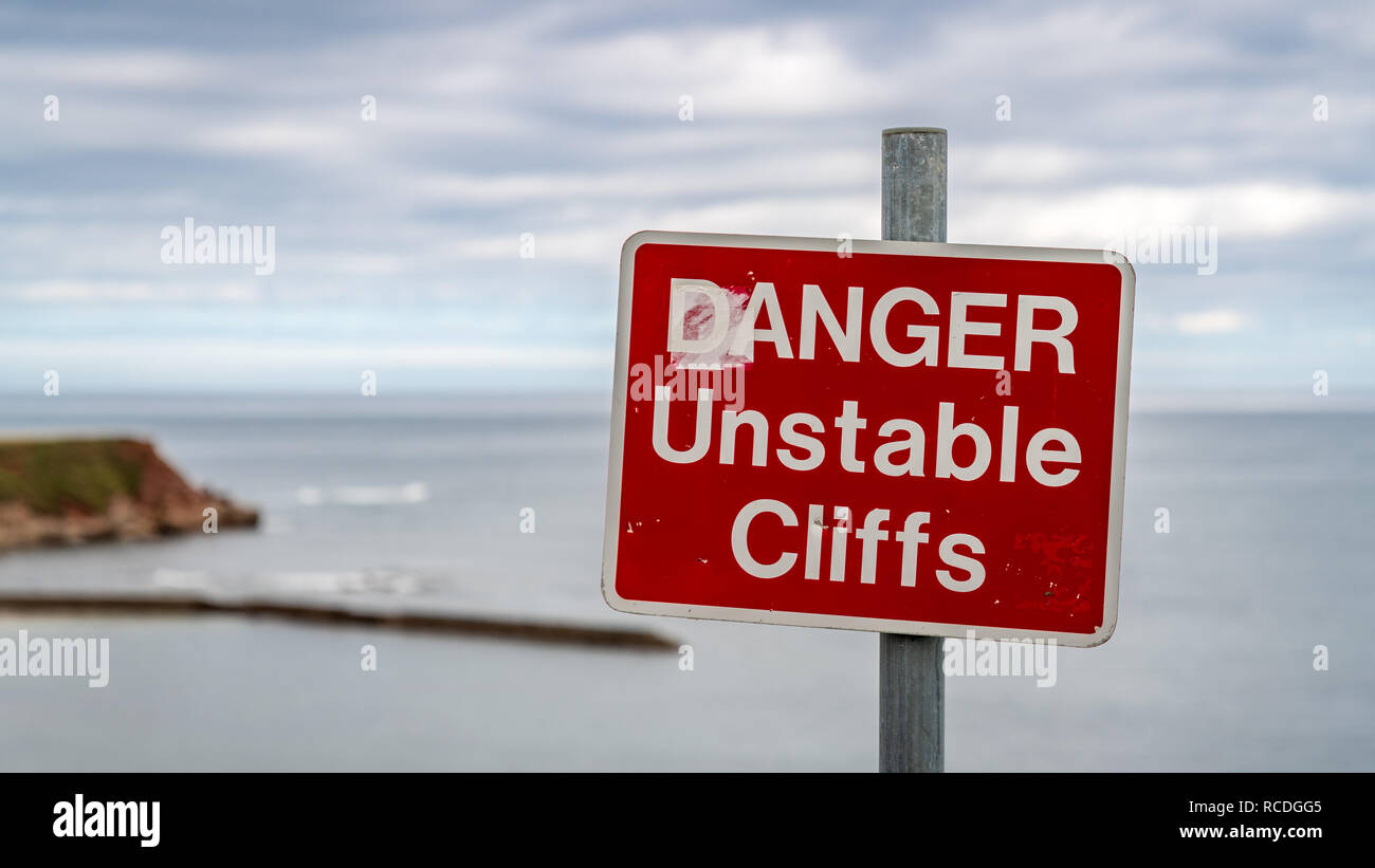 Sign: Danger unstable cliffs, with cliffs in the blurry background ...