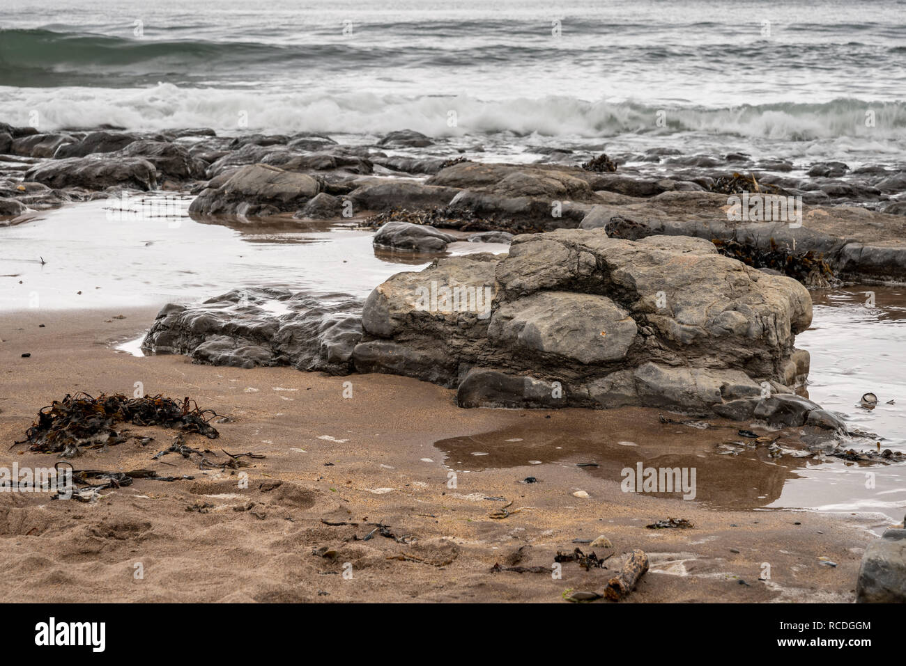 Large stones on a beach with water approaching in the background, seen ...