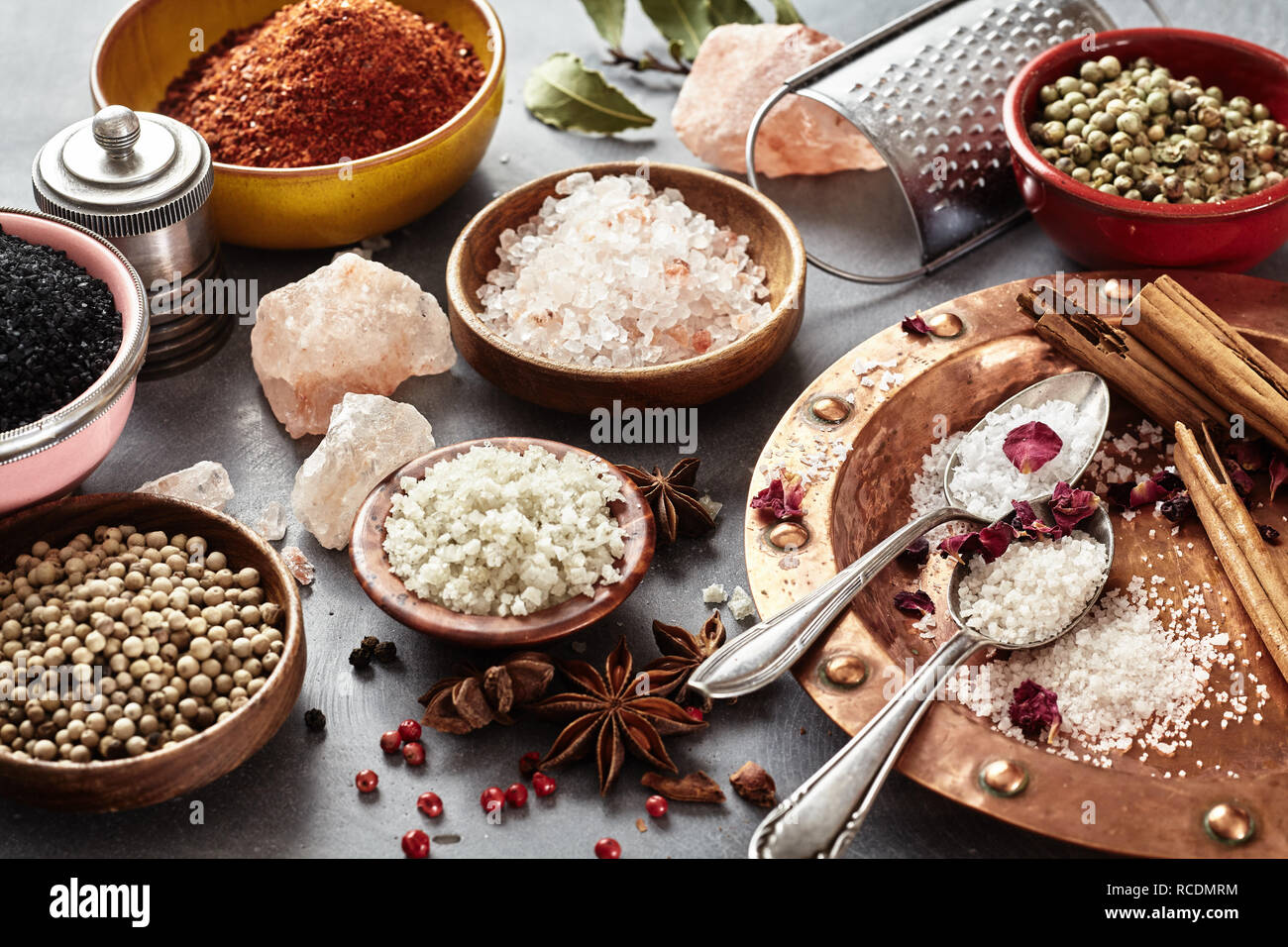 A variety of natural cooking salt in bowls with peppercorns, herbs and ...