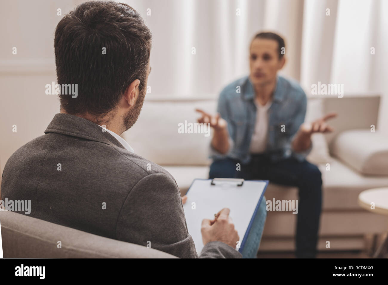 Psychologist wearing grey jacket listening to his anxious client Stock ...