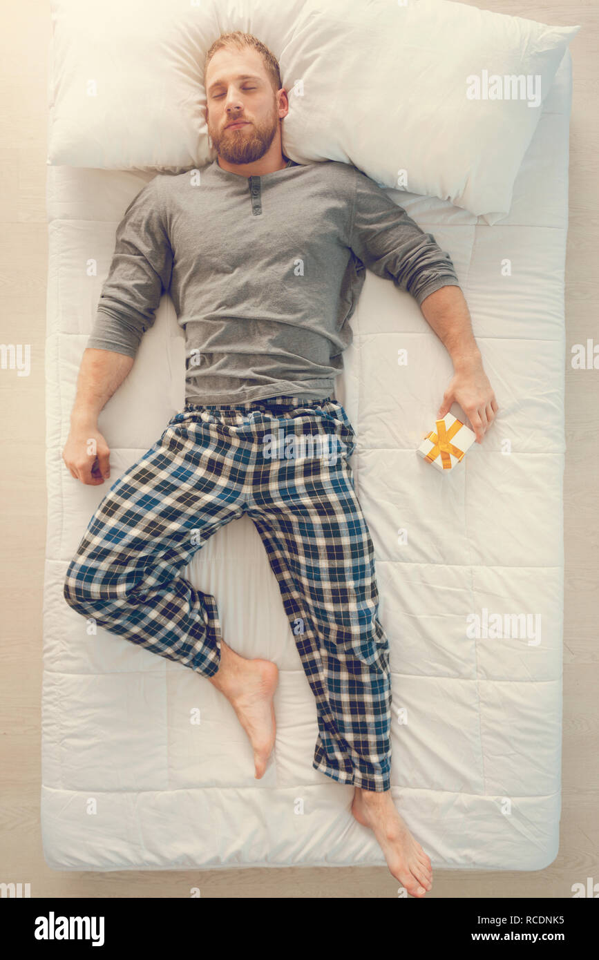 Small surprise. Young bearded man sleeping on his bed while keeping a ...