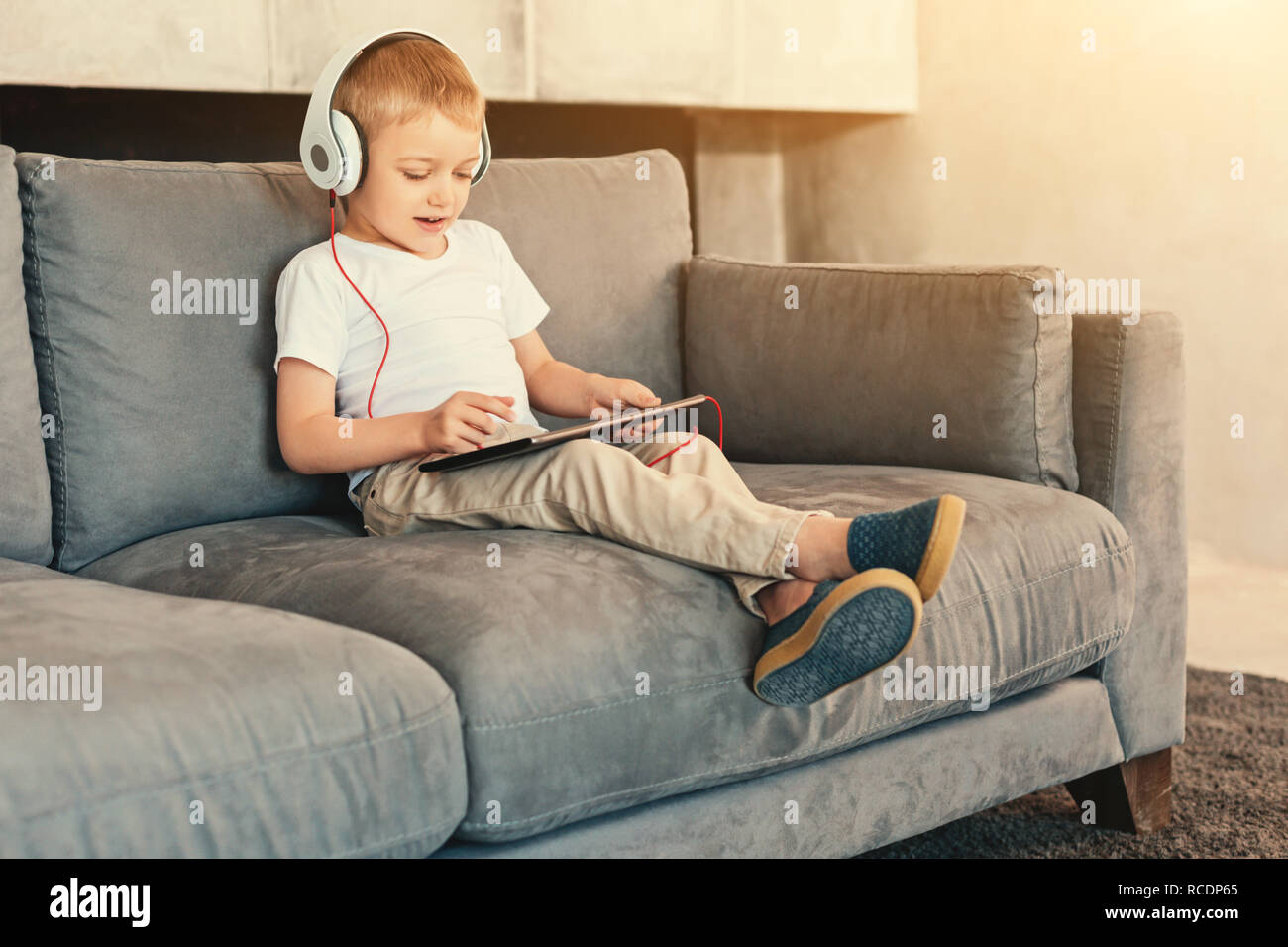 Technology lover. Cute little boy sitting on the sofa and playing a ...