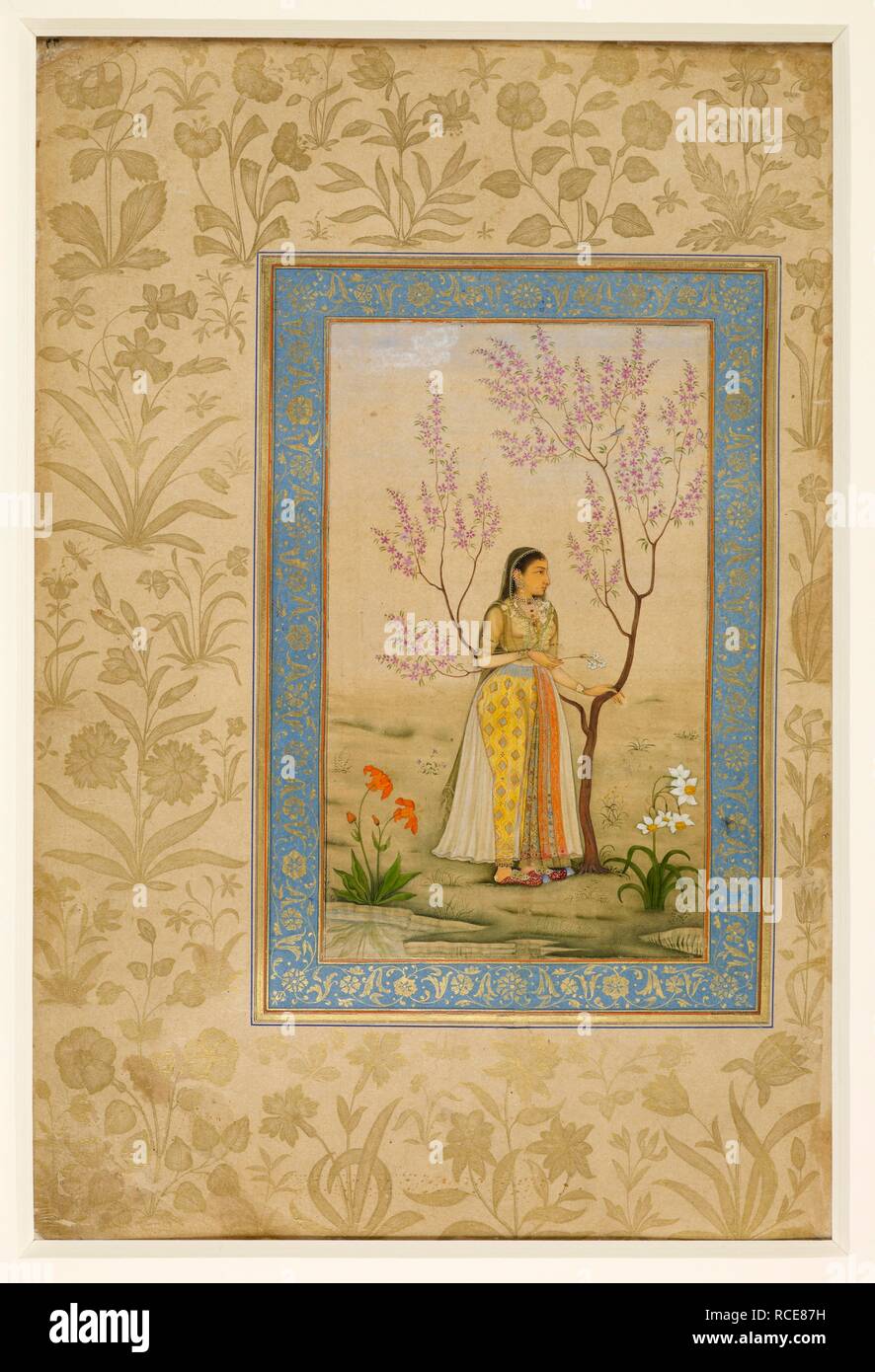 A young lady stands beneath a blossoming tree holding a sprig of ...