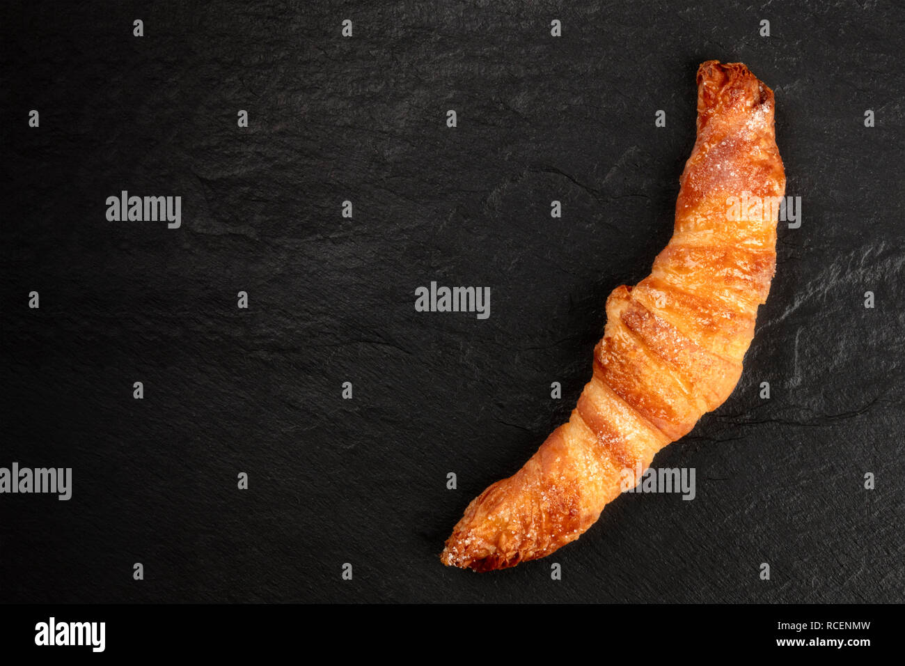 A croissant on a black background, shot from above, with copy space ...