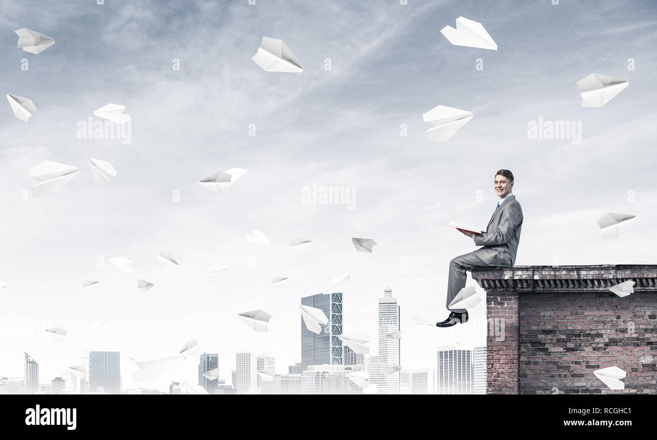 Man on roof edge reading book and cityscape at background Stock Photo ...