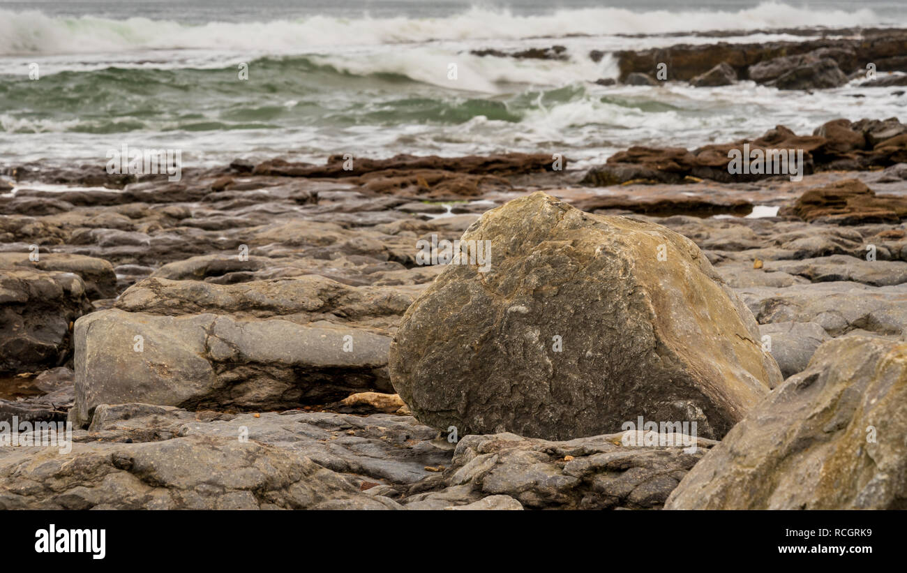 Large stones on a beach with water approaching in the background, seen ...