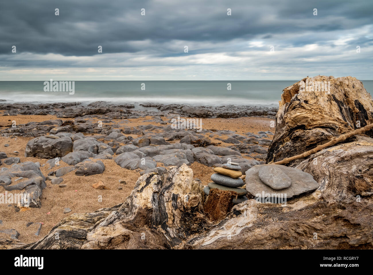 A stone pile on a tree trunk, under a dramatic sky on a stony beach ...