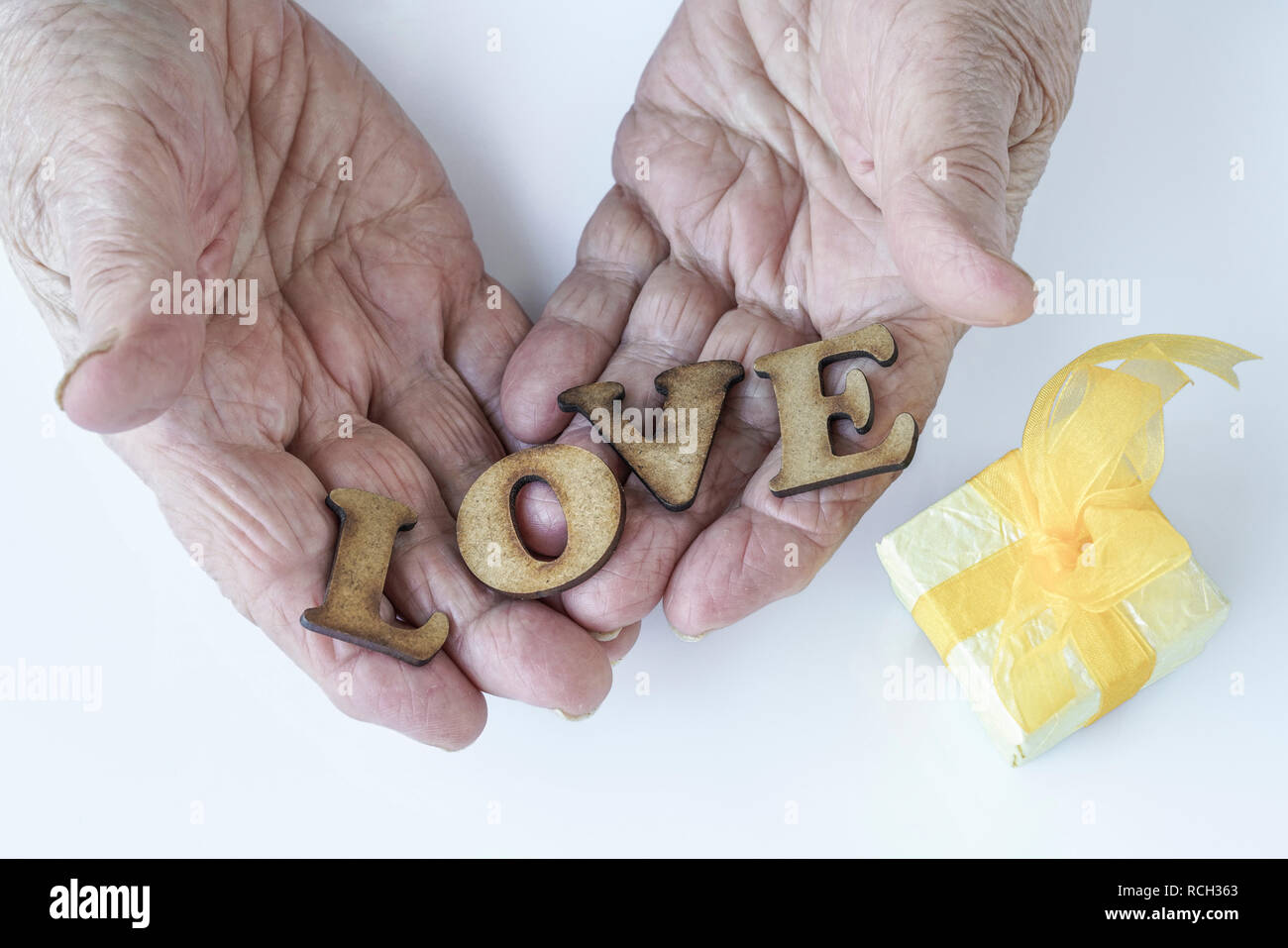 Wrinkled hand of a senior person and yellow gift pack on white Stock ...