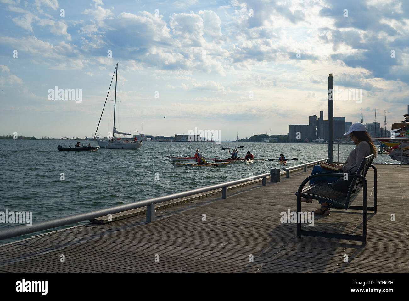Side profile of a woman sitting on a bench lakeside reading a book in ...