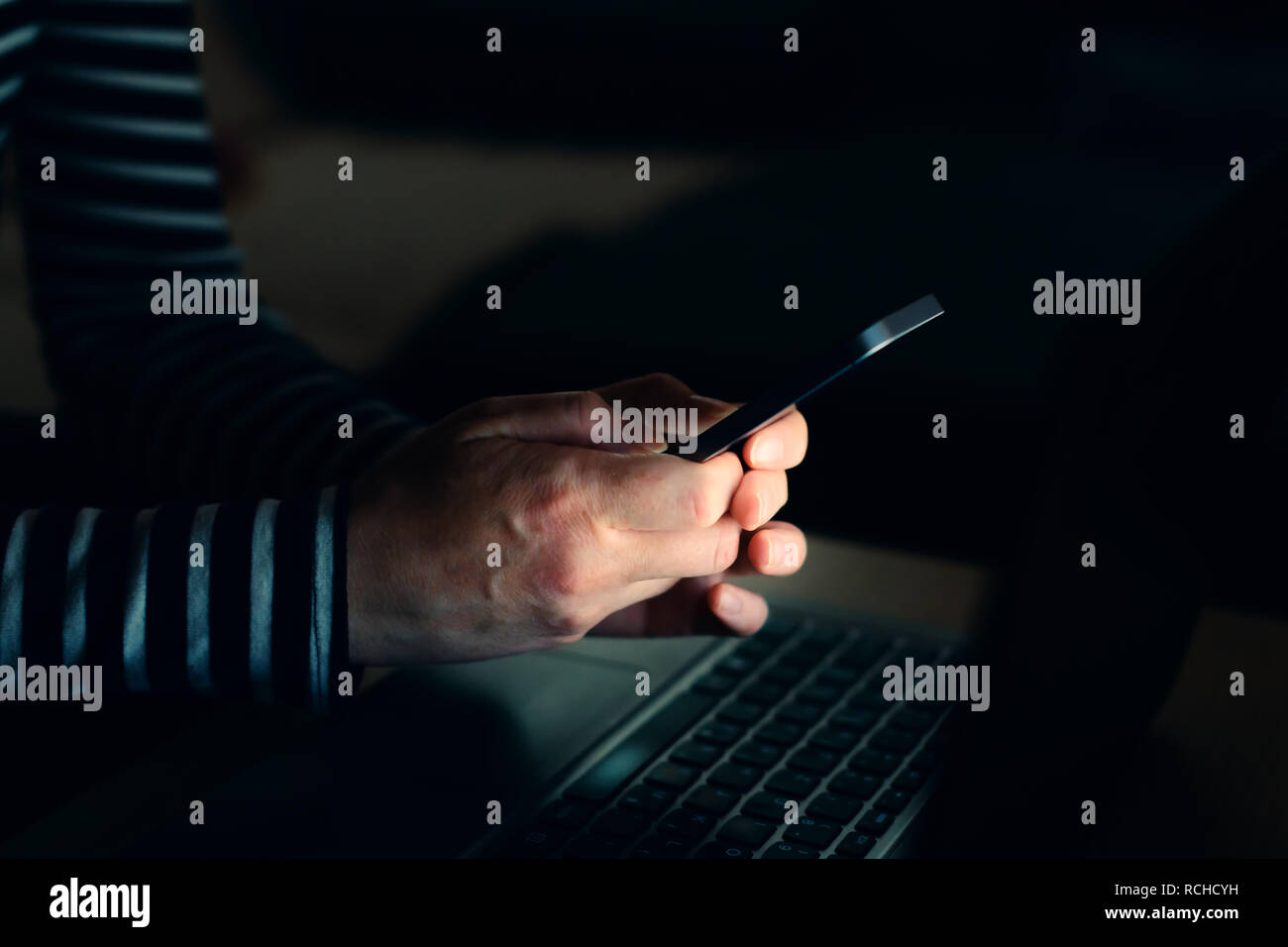 Using smartphone and laptop computer late at night, low key image of ...