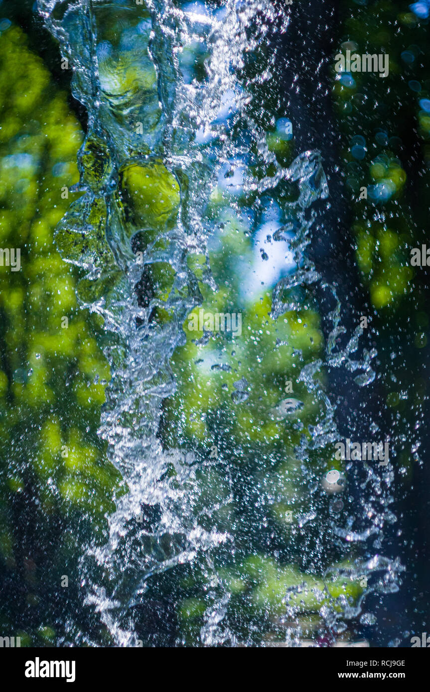 transparent falling water vertical flows against a blue sky and green ...