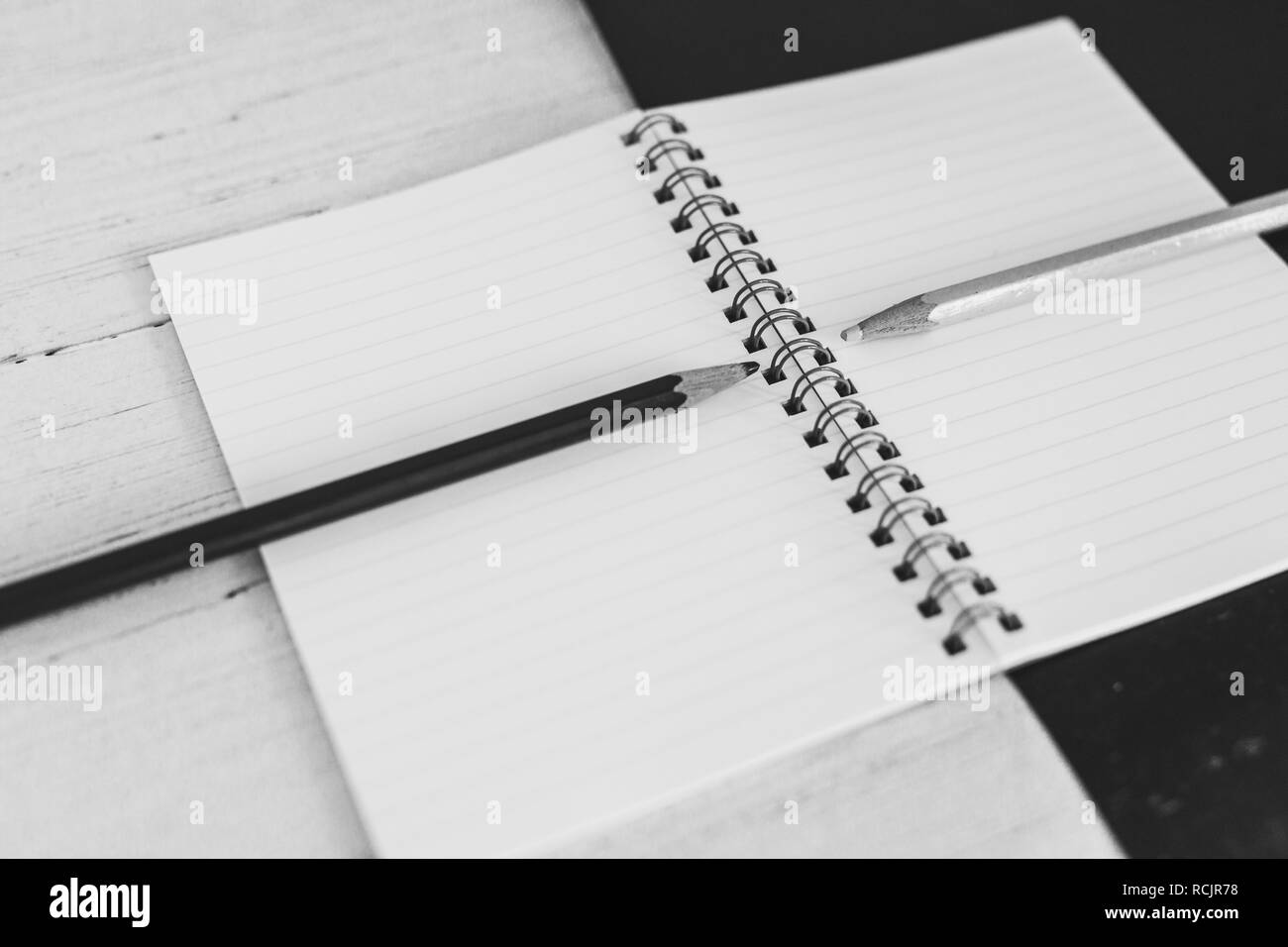 open notepad on black and white background with pencils of the opposite ...