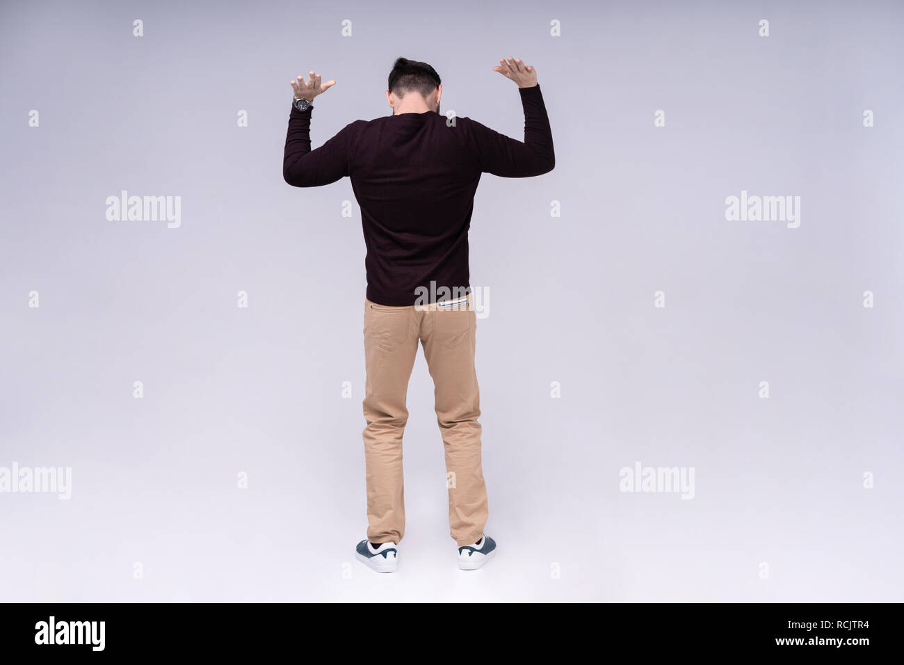 back view of a casual man standing with hands up on white background ...
