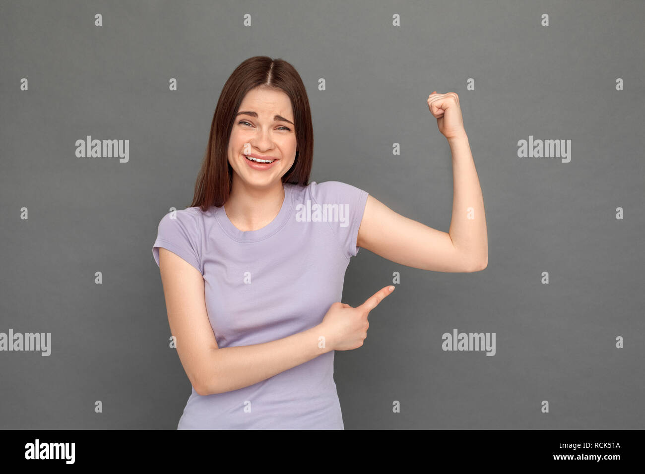 Young girl standing isolated on grey wall pointing at arm muscle ...