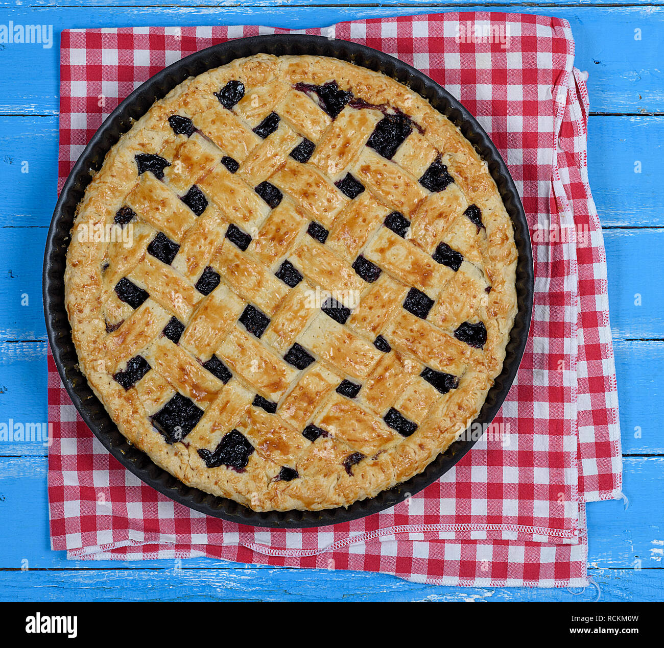 baked round black currant cake on an iron plate, top view, wooden blue ...
