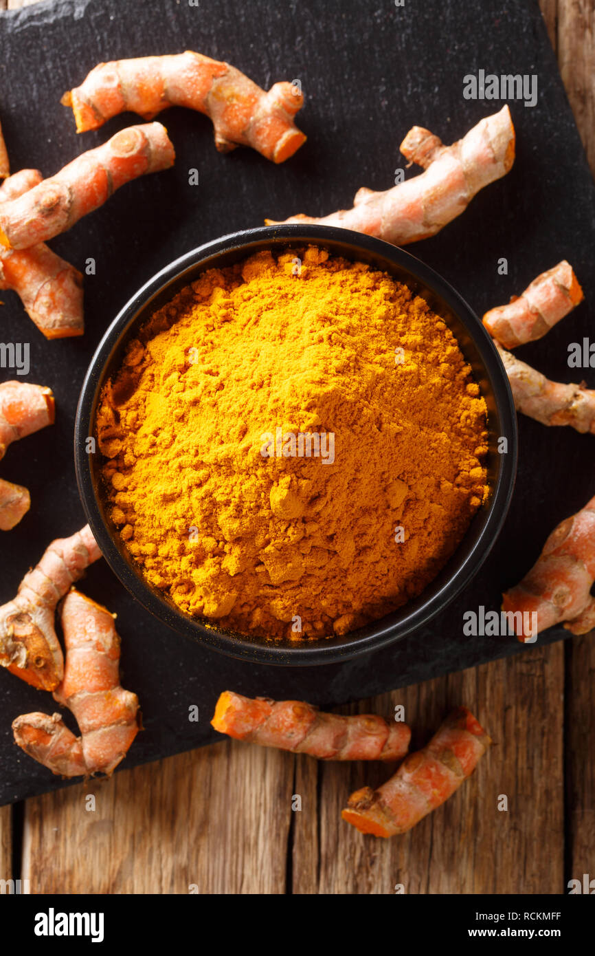 Fresh turmeric spice in a bowl and root close-up on the table. Vertical ...