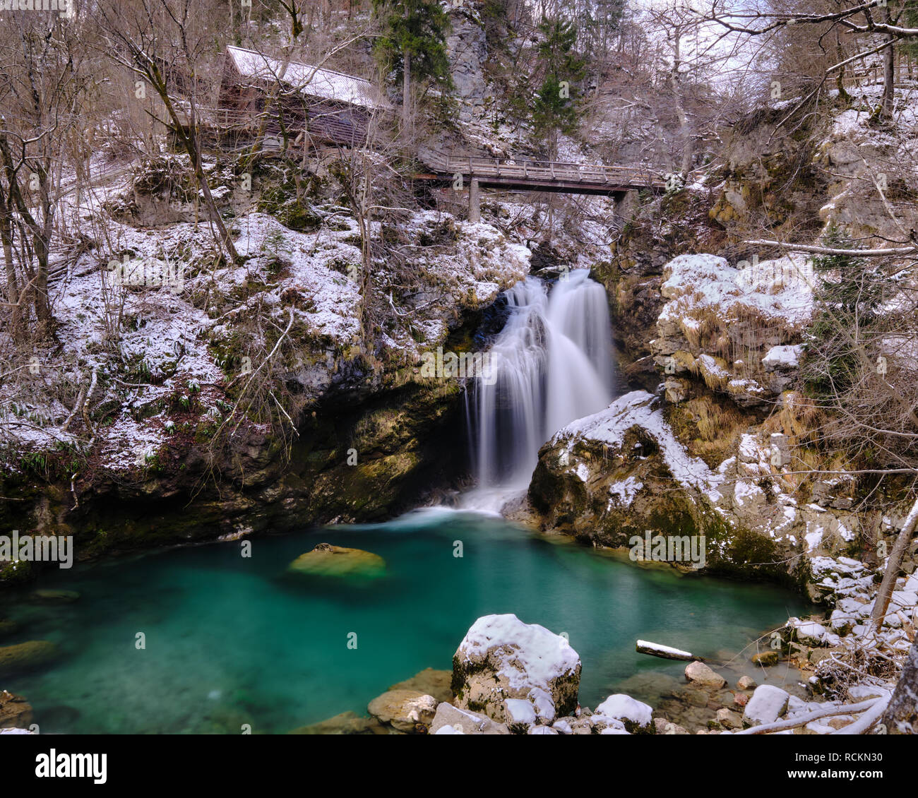 Cabin in Vintgar gorge in winter. Waterfall dropping from under a ...