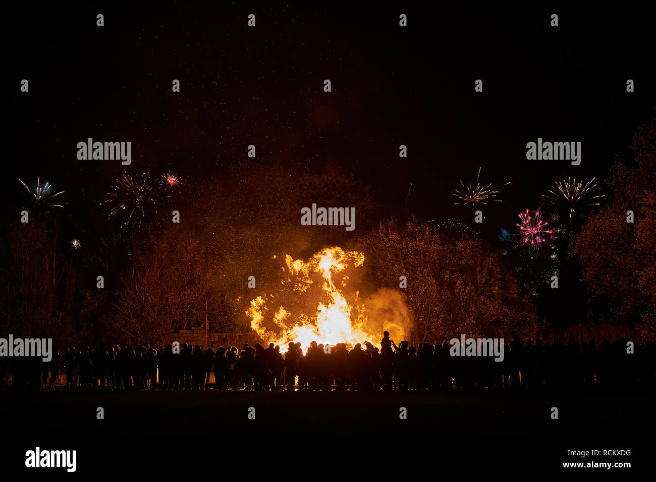 A crowd of people standing, watching a bonfire with fireworks in the ...