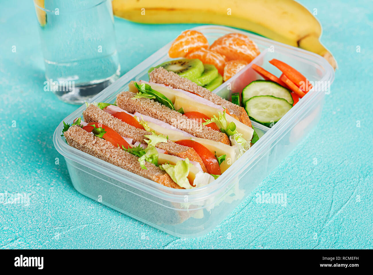 School lunch box with sandwich, vegetables, water, and fruits on table ...