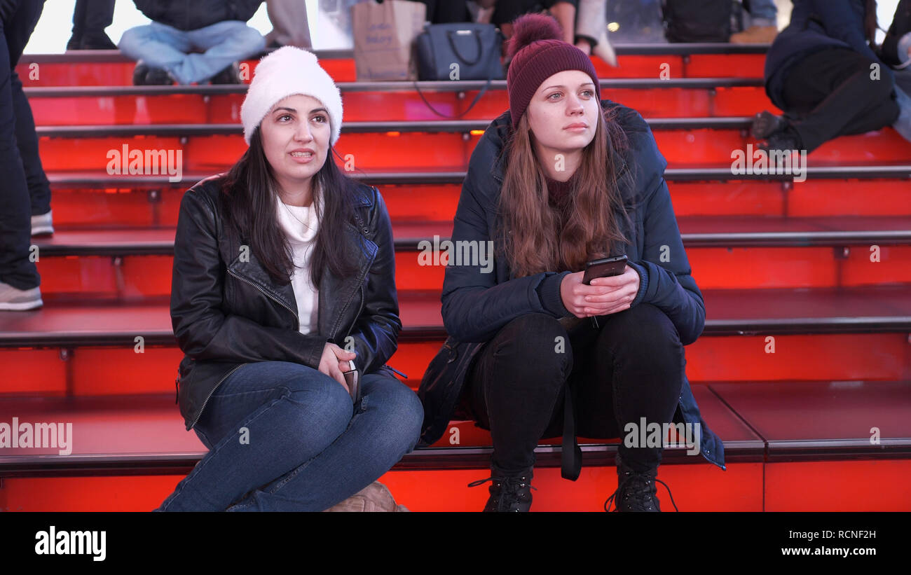 Two girls at Times Square by night sit on the famous red steps Stock ...