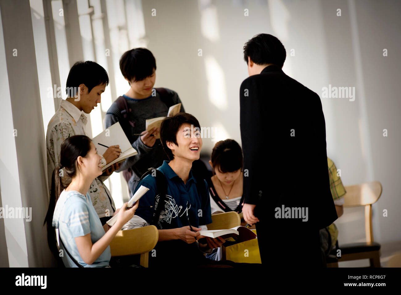 Teenage students talking with their mid-adult teacher in a classroom ...