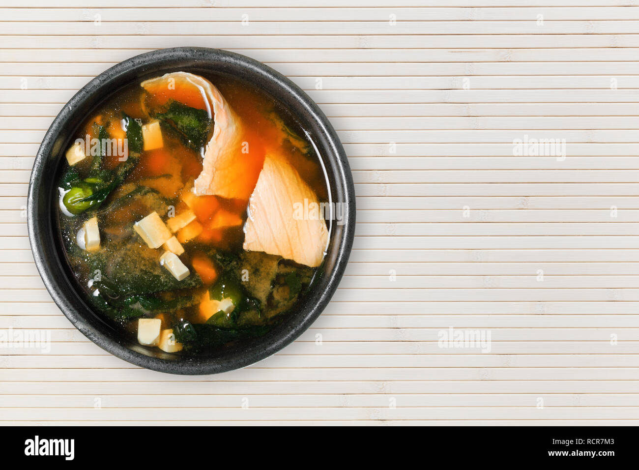 Appetizing soup with salmon, tofu and seaweed. Wooden background with ...