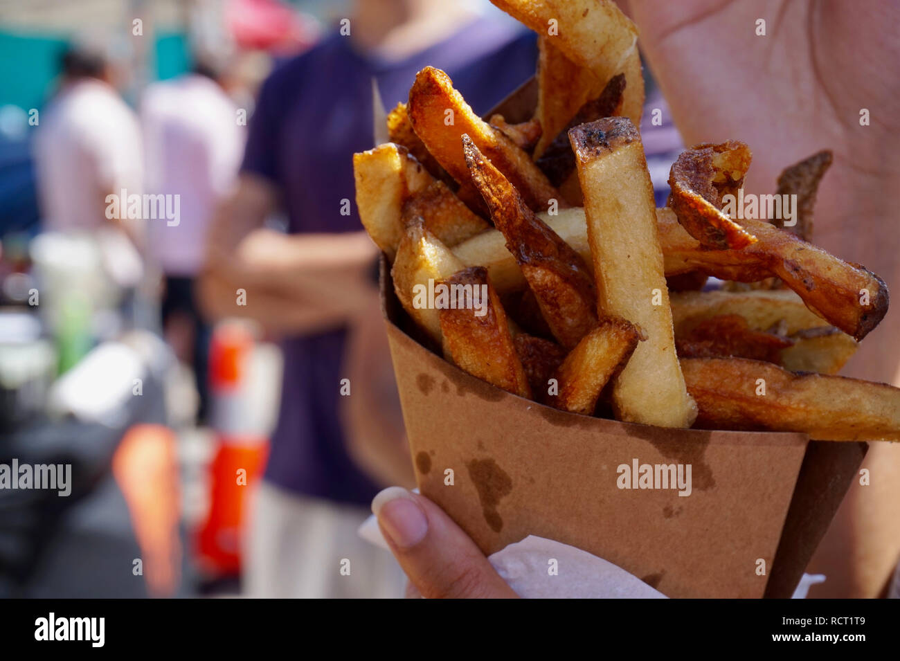 Holding french fries to go in a paper cone take out carrier, outdoors ...