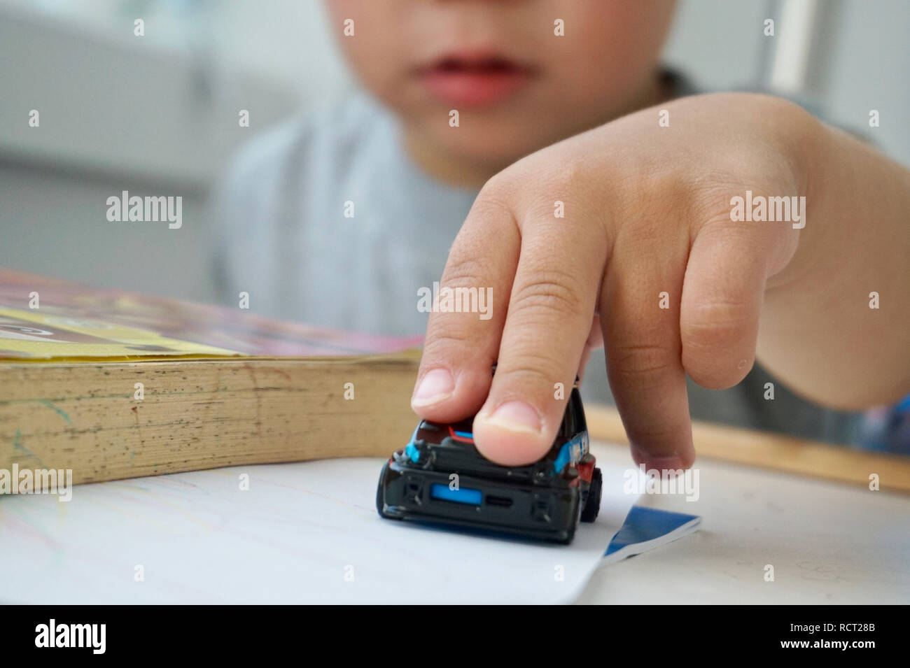 Toddler fingers pushing a toy car on a play table. Partial face showing ...