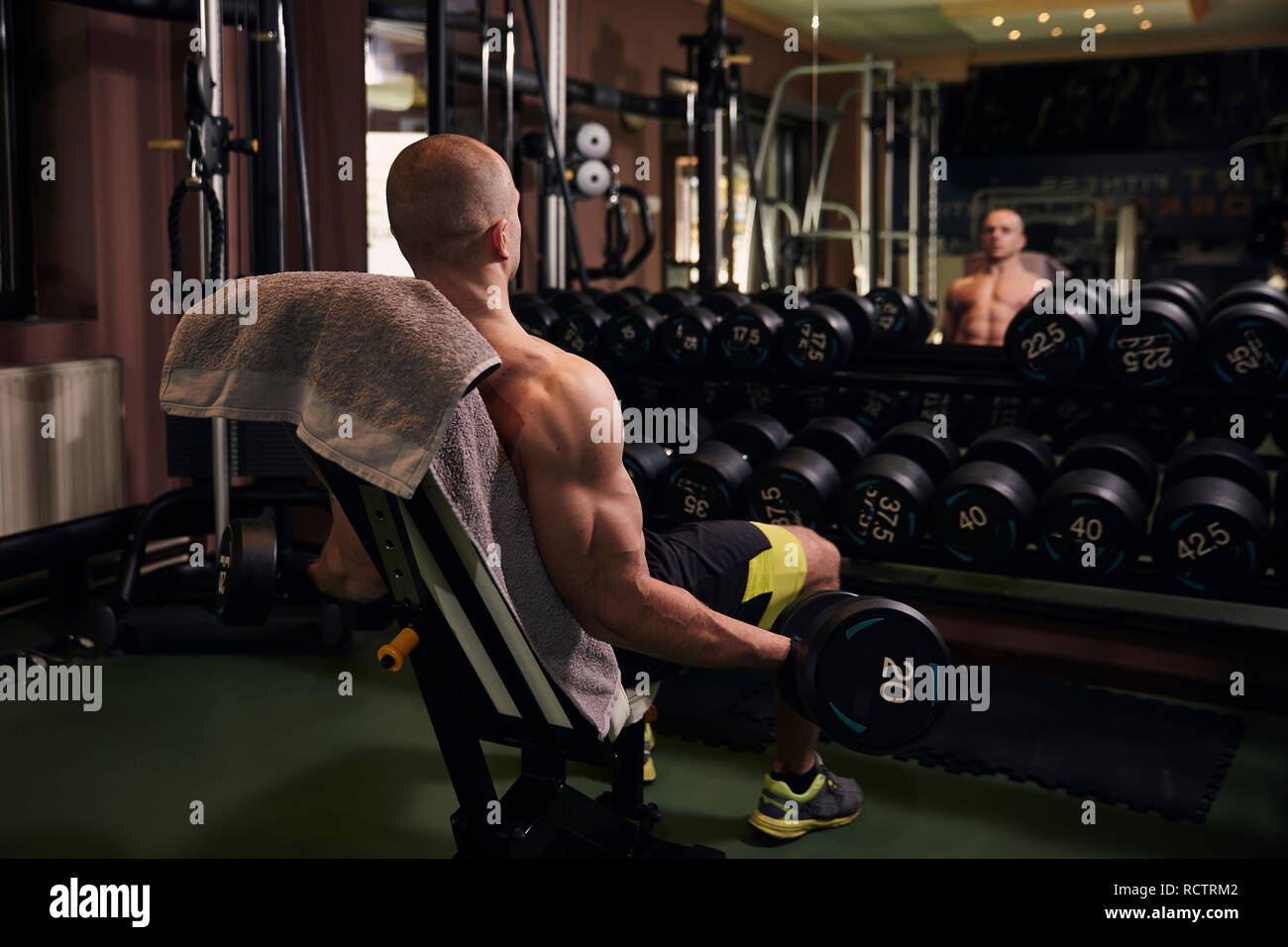 One muscular man bodybuilder, rear view (from behind), sitting on bench ...