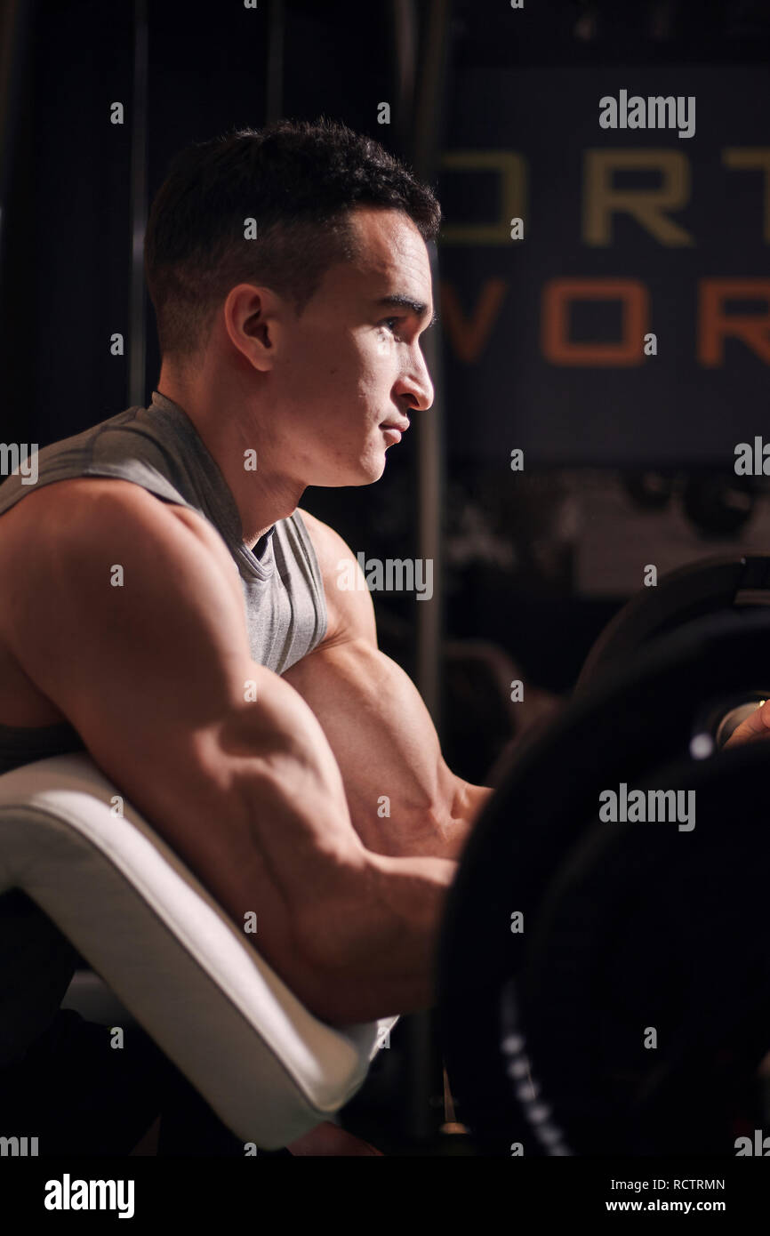 one young man, side view of him exercising in gym, muscular bicep and ...