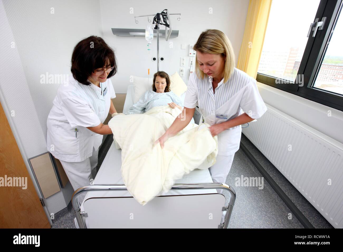 Patient lying in a hospital bed, nurses making the bed, single room ...