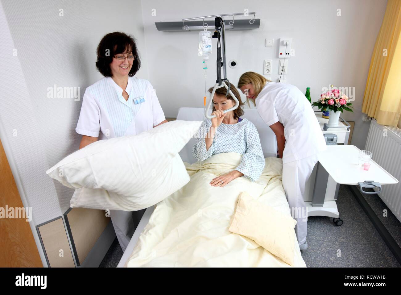 Patient lying in a hospital bed, nurses making the bed, single room ...