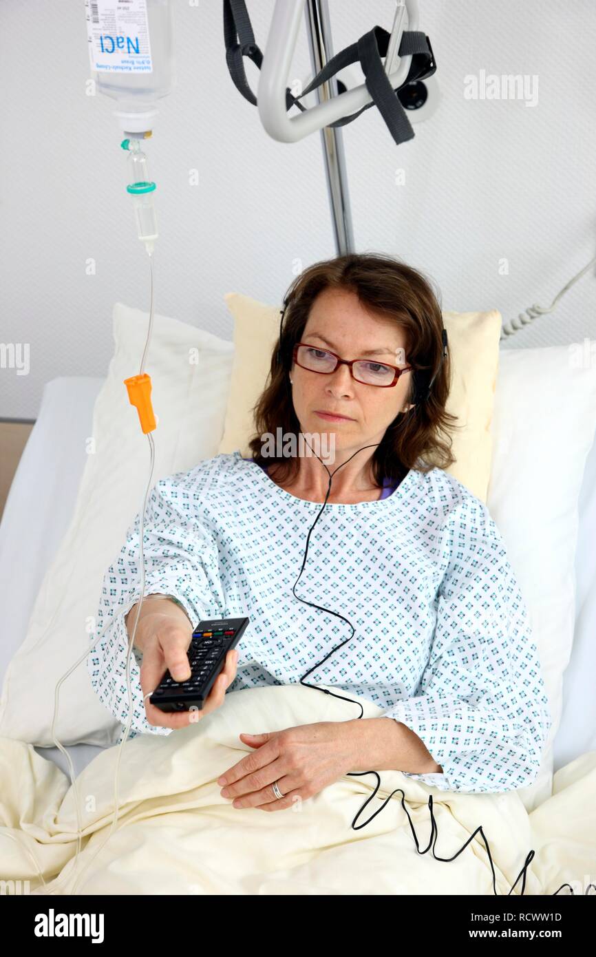 Patient lying in a hospital bed operating the TV with a remote control ...