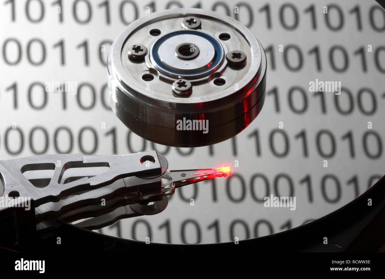 Computer hard drive, opened, read-write head on the disk, binary numbers reflected in the disc ...
