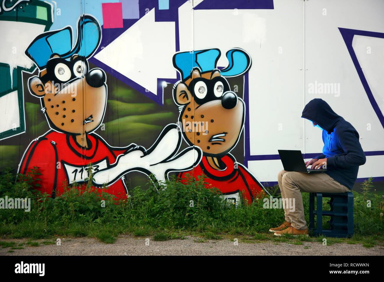 Man surfing on a laptop computer in front of a graffiti covered wall ...