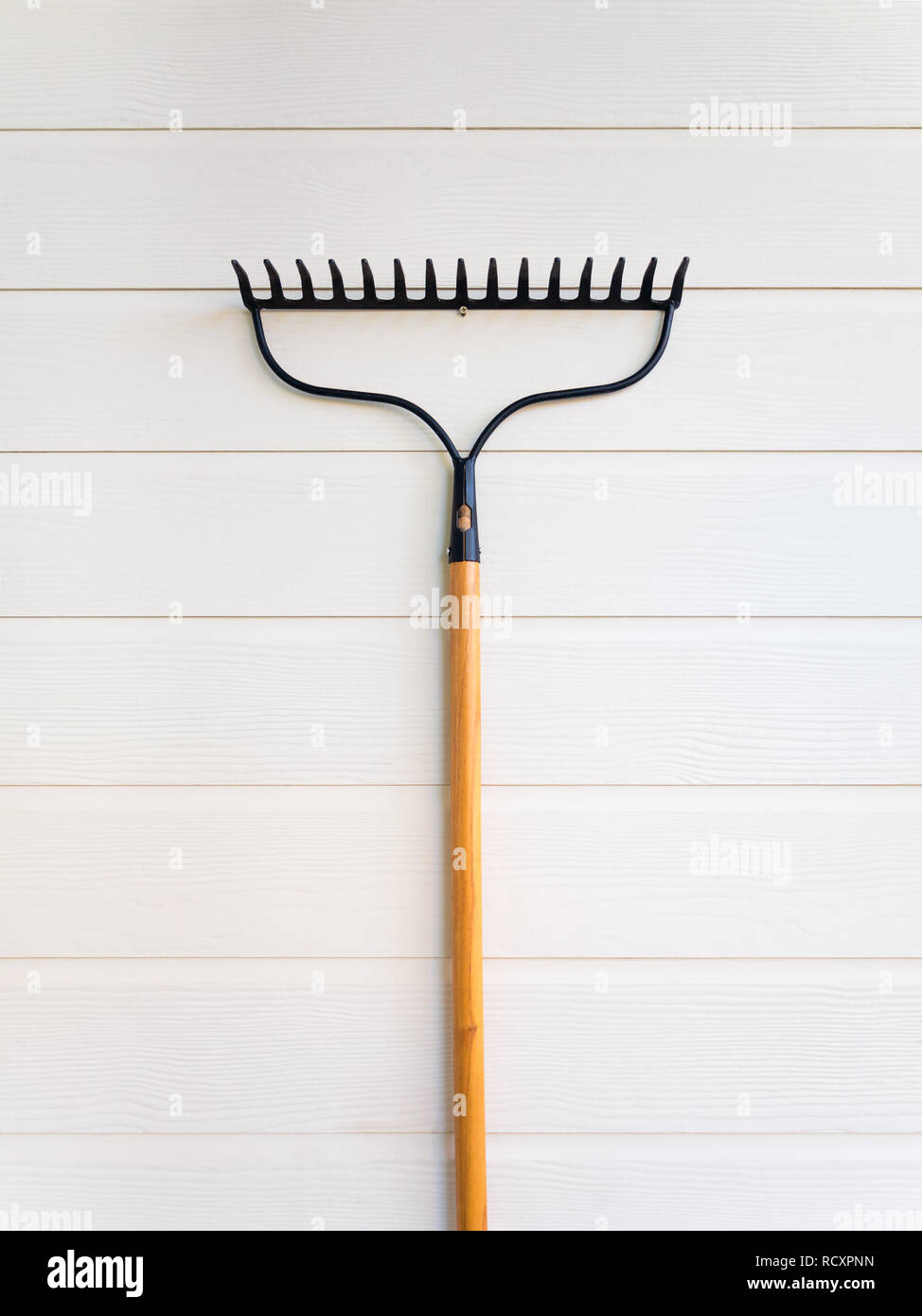 Minimalist image of new rake hanging on clean white wooden texture wall ...