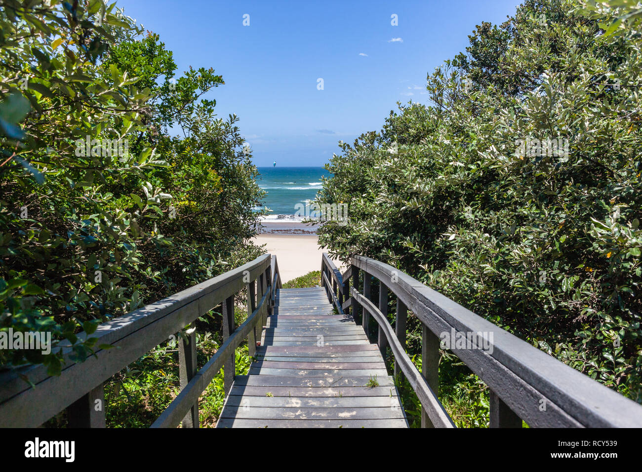 Beach entrance walking stairs towards windy ocean with distant kite ...