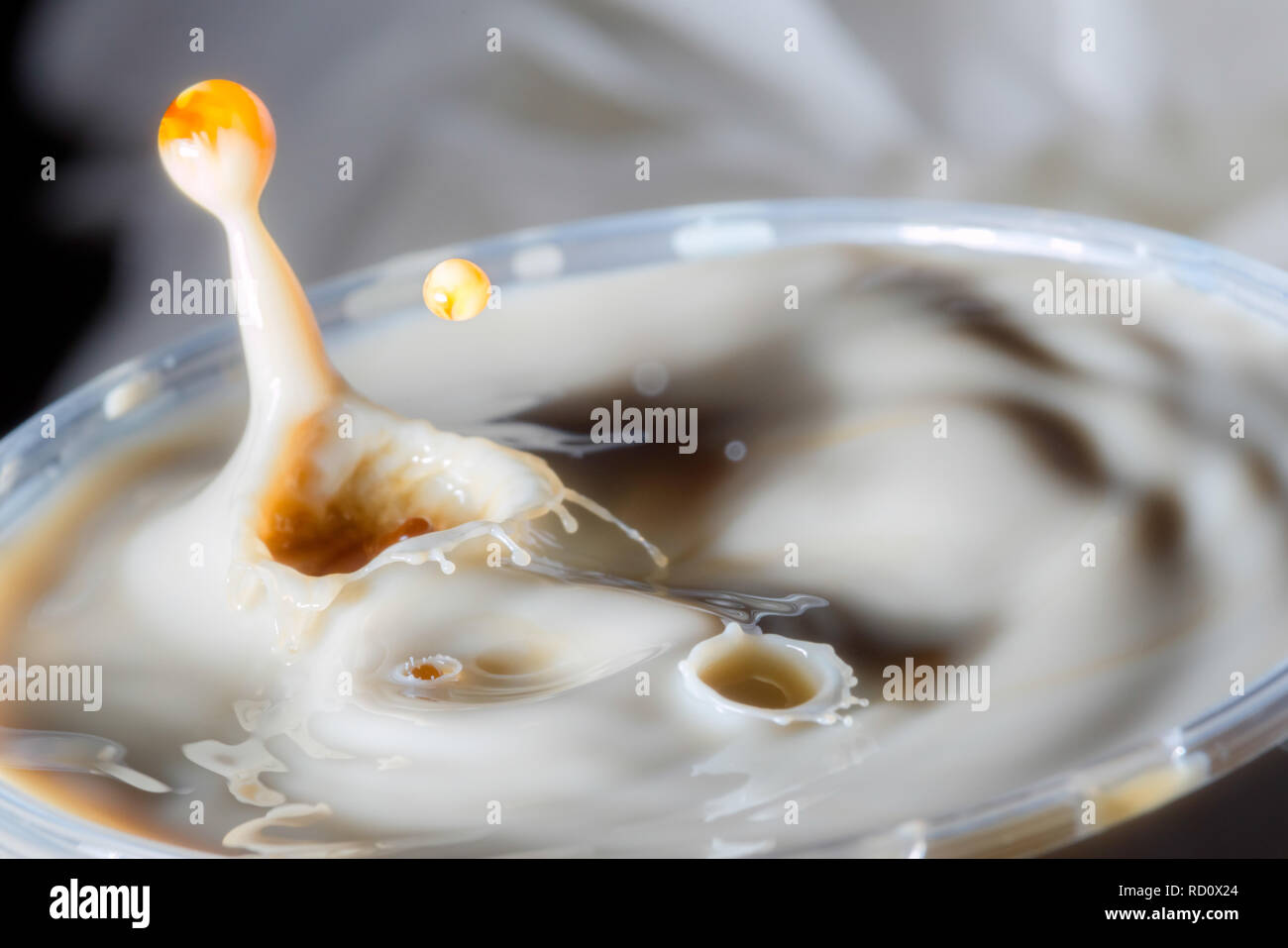 high speed photograph of a caramel milk drop on dark background in the ...