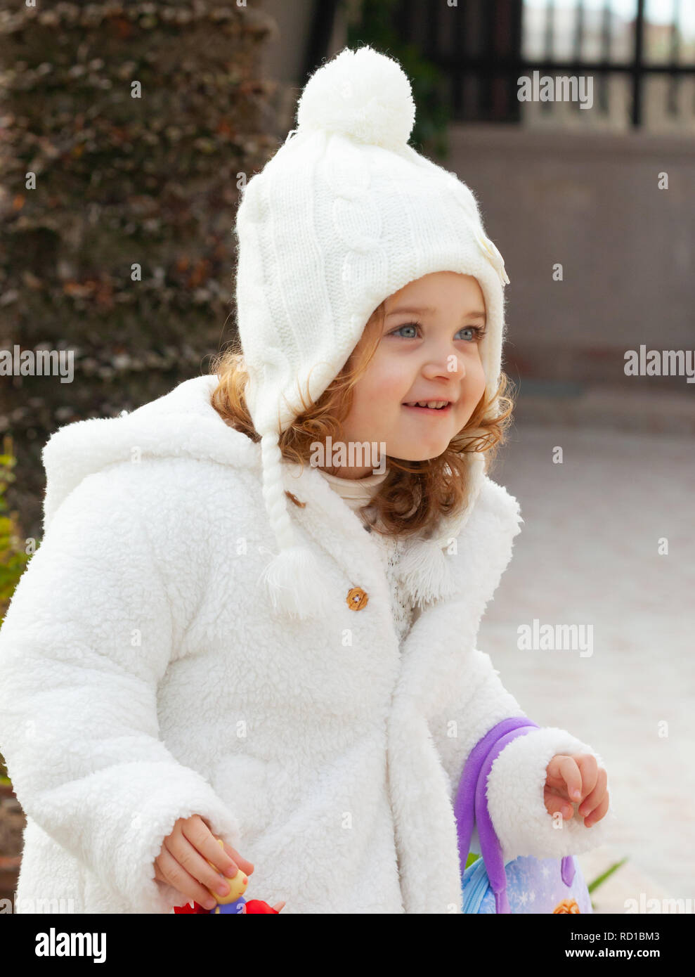Pretty girl with wool hat and and white coat in a garden at winter ...