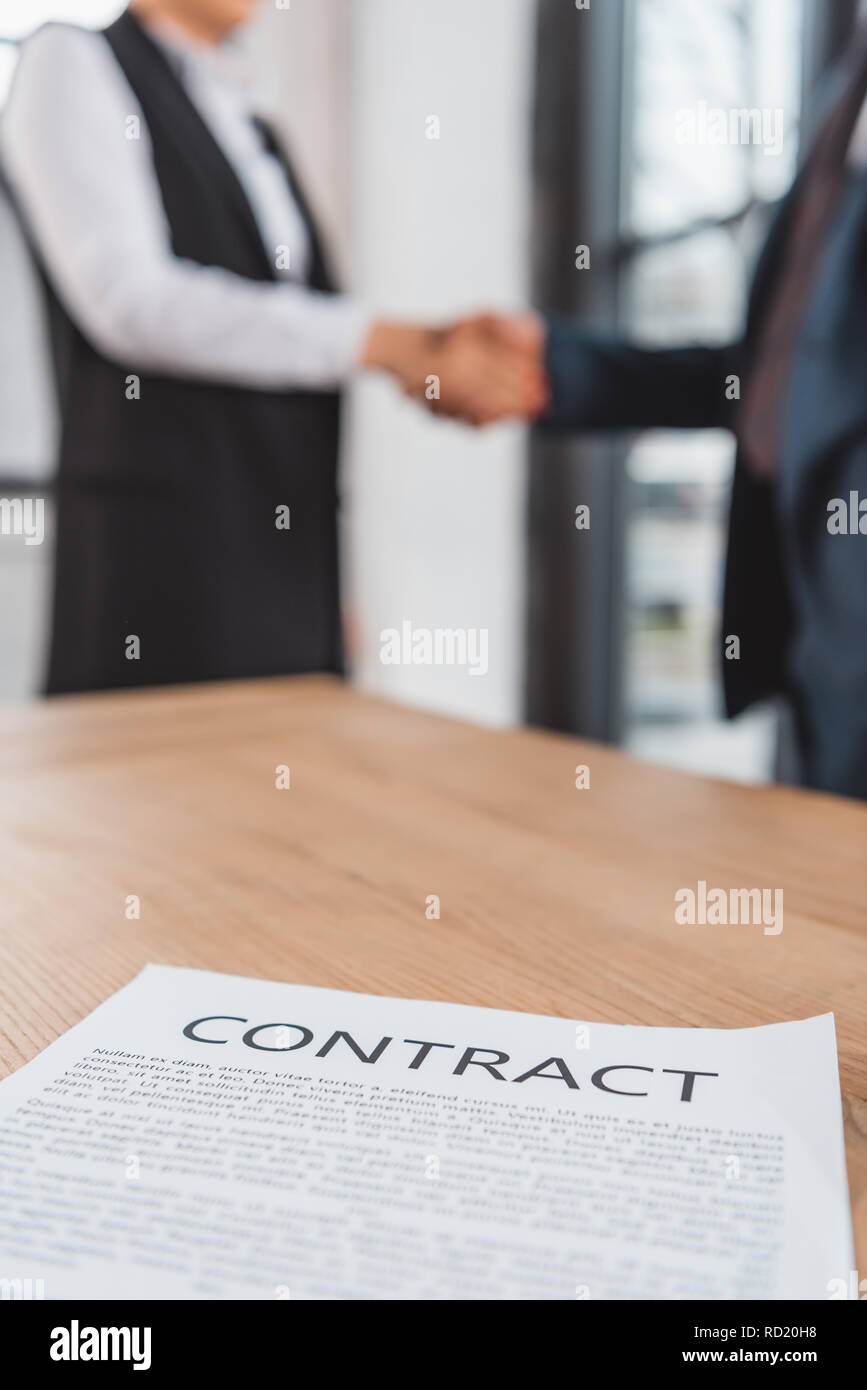 close-up view of contract on table and business people shaking hands ...