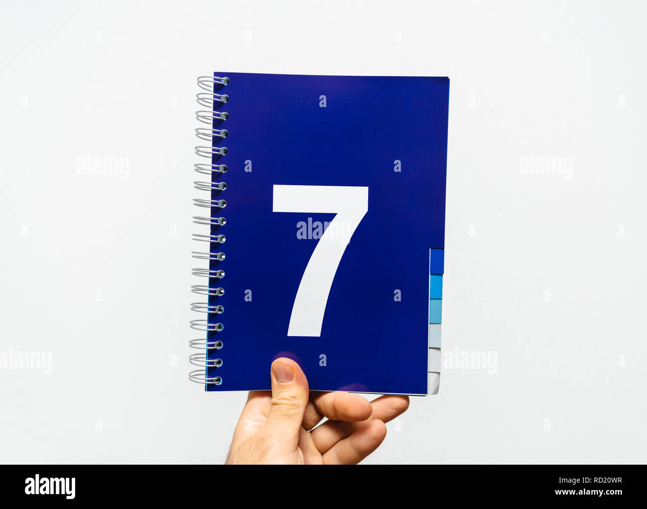 Male hand holding notebook with big number 7 printed on blue color ...