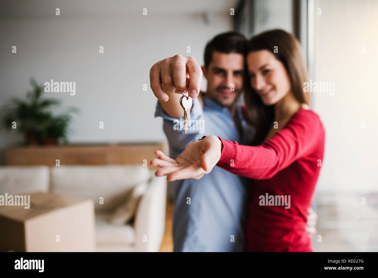 A young couple with a key and cardboard boxes moving in a new home ...