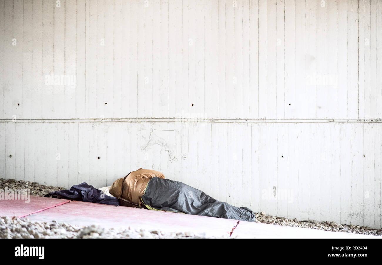 A rear view of homeless beggar man lying on the ground outdoors in city ...